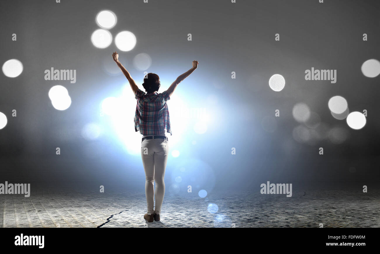 Back view of girl with hands up standing in stage lights Stock Photo ...
