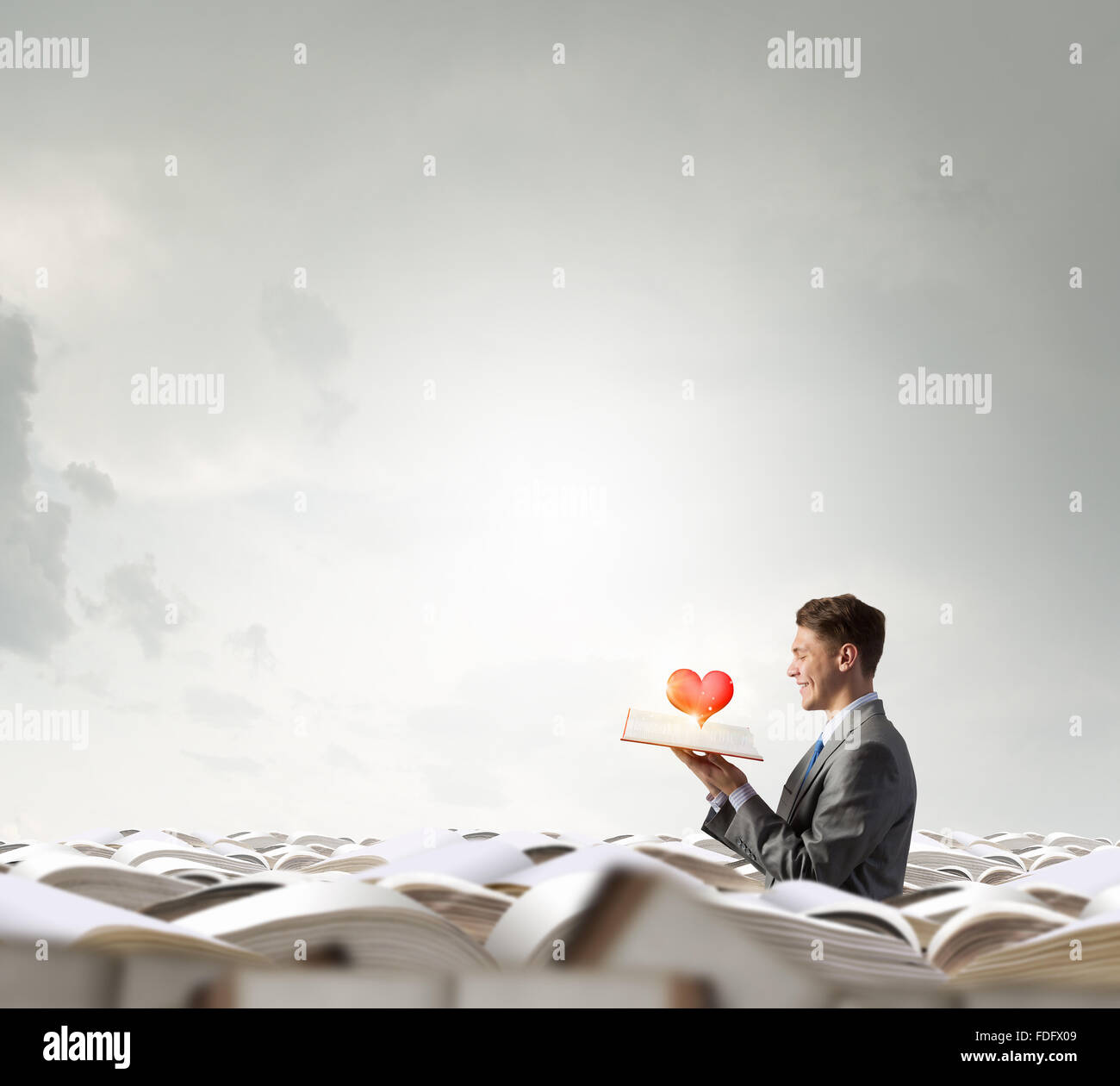 Young man in pile of books with one in hand Stock Photo - Alamy