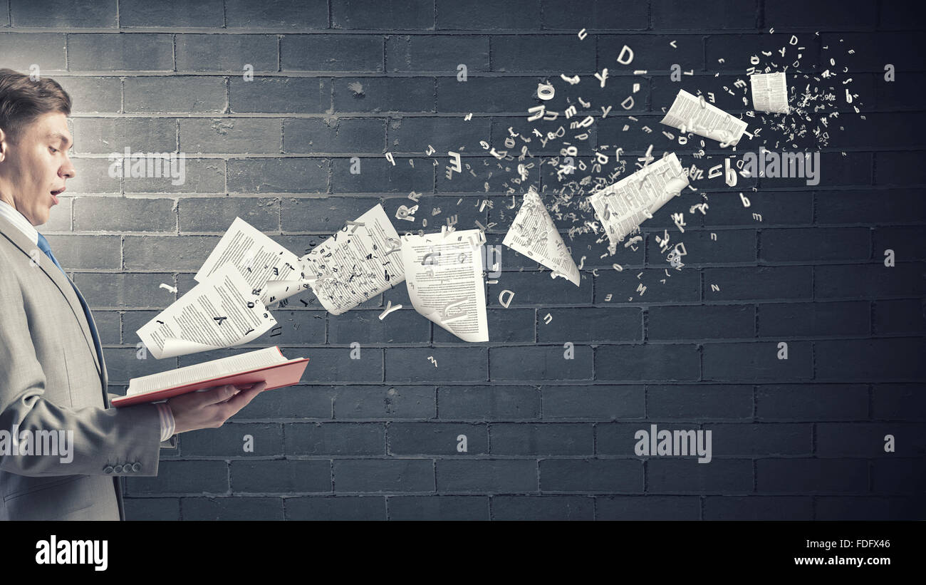 Young businessman with opened book in hands and pages flying in air ...