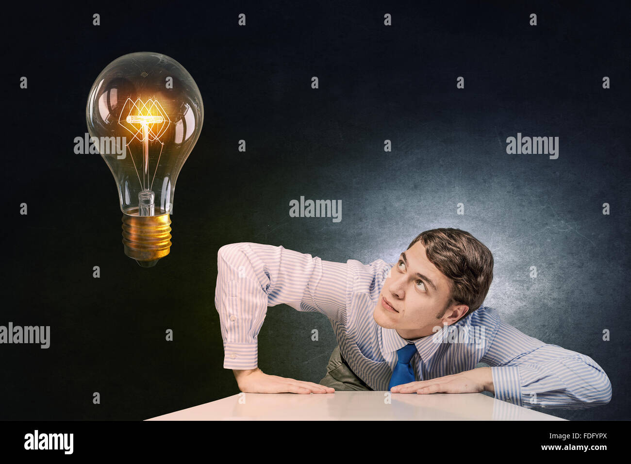 Young man leaning on table and looking at light bulb Stock Photo - Alamy