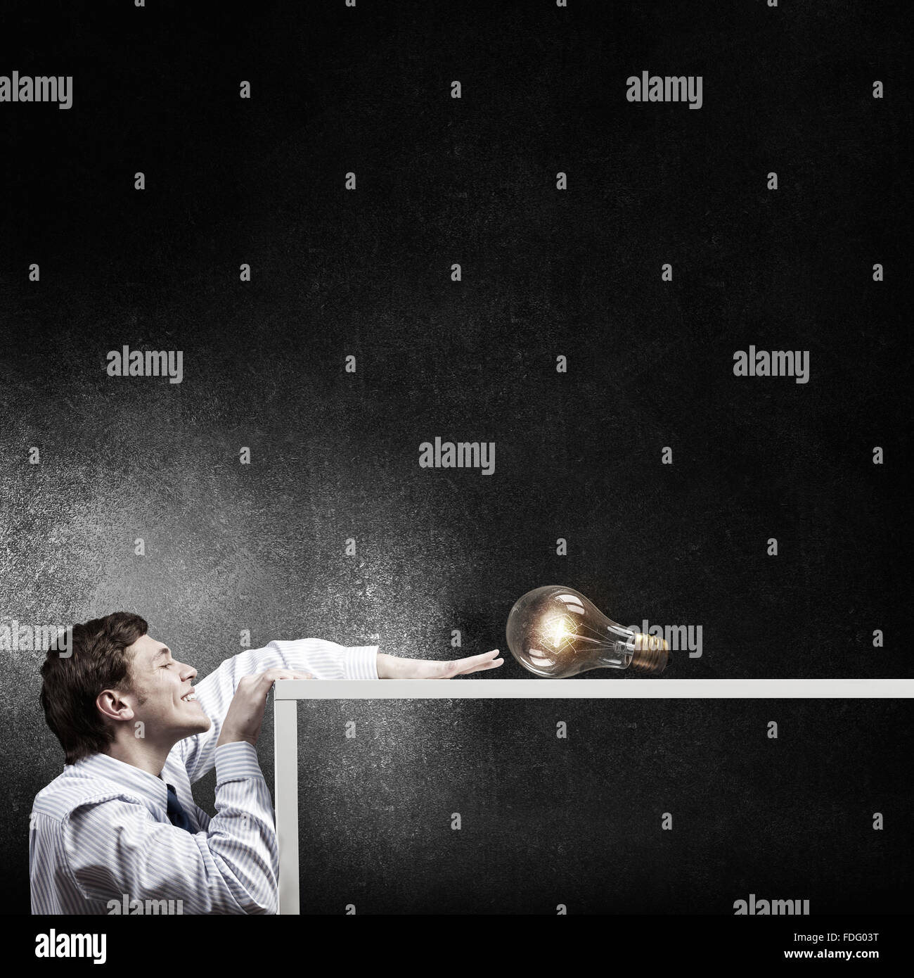 Young man looking from under table at glass light bulb Stock Photo - Alamy