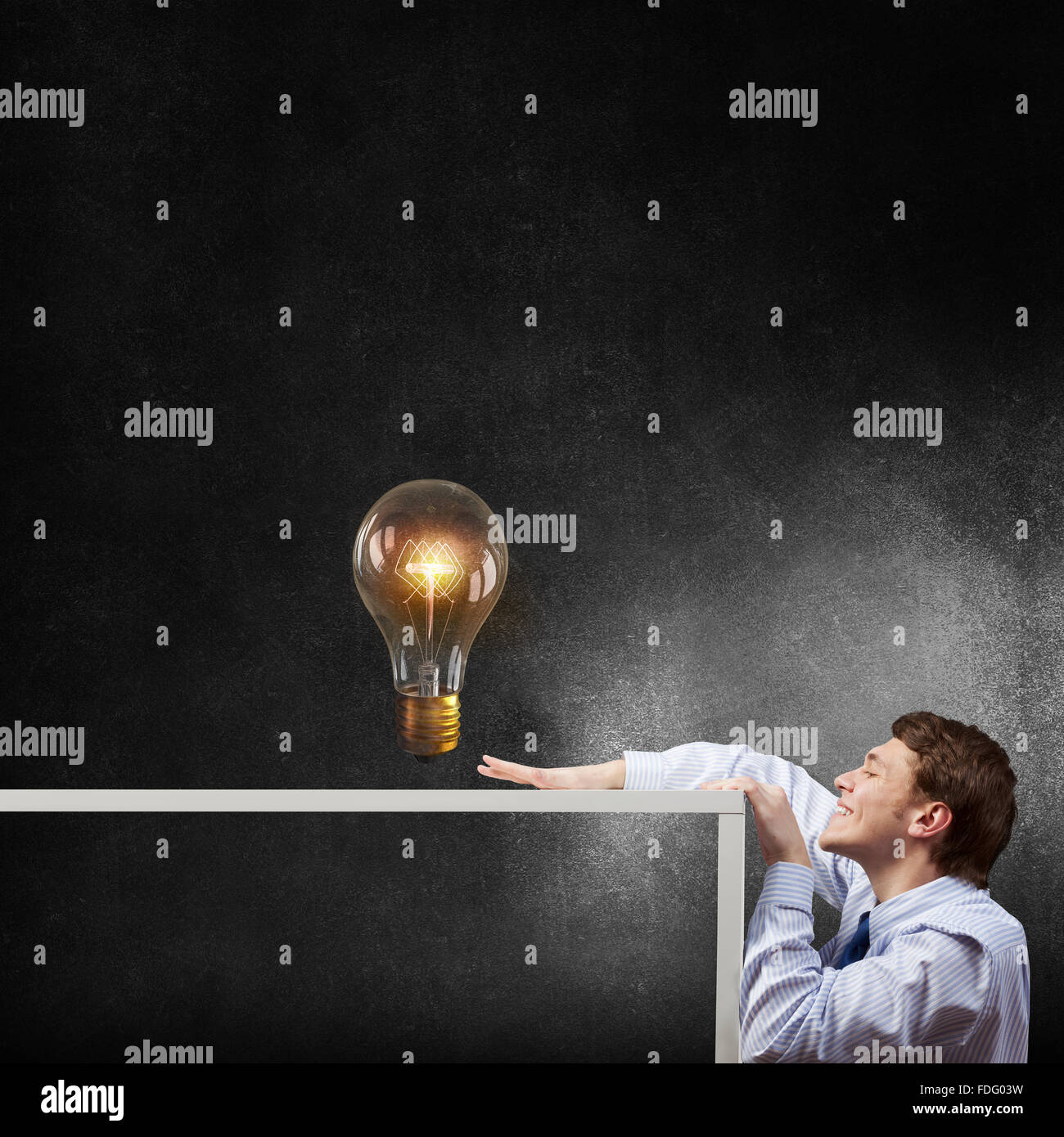 Young man looking from under table at glass light bulb Stock Photo - Alamy