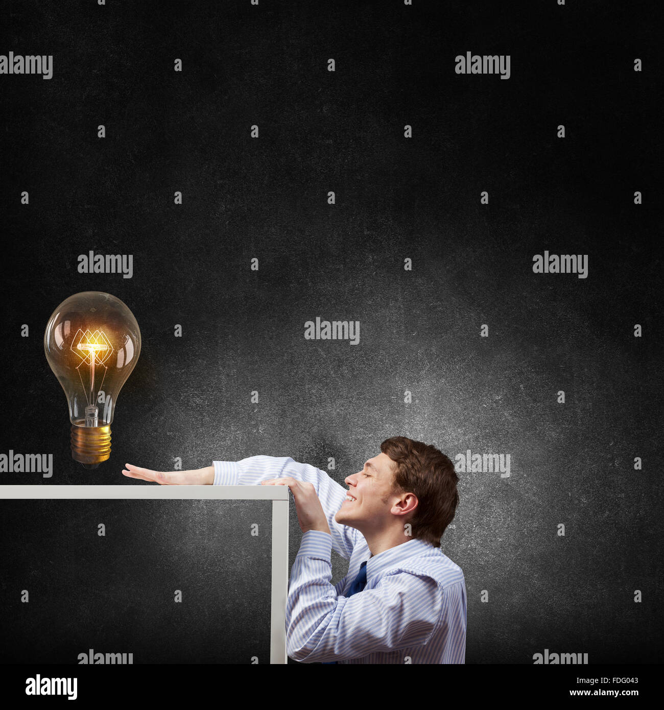 Young man looking from under table at glass light bulb Stock Photo - Alamy
