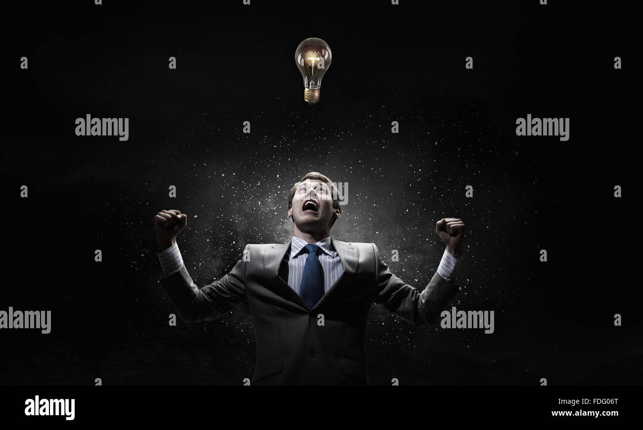 Young businessman with hands up screaming at light bulb above his head ...