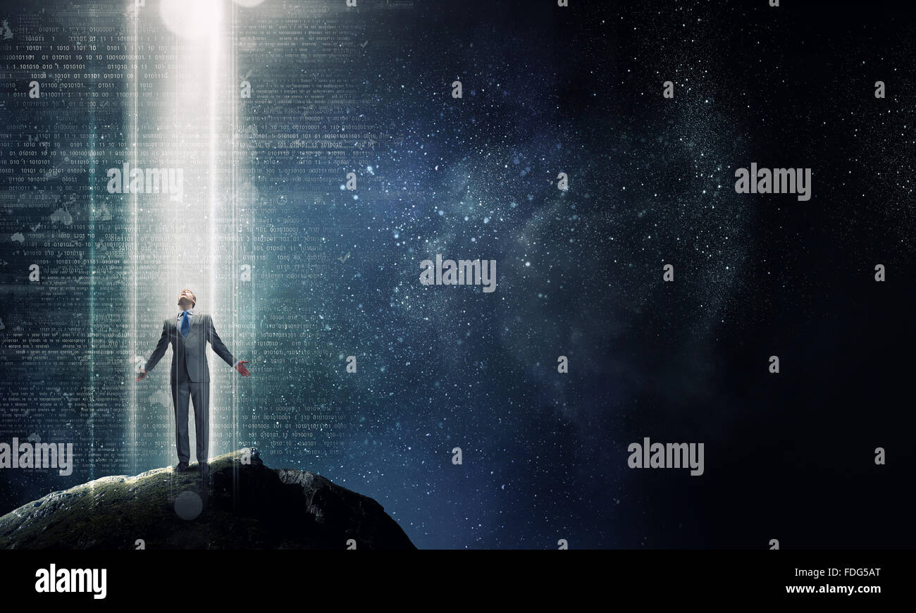 Businessman with hands spread apart standing in light coming from above ...