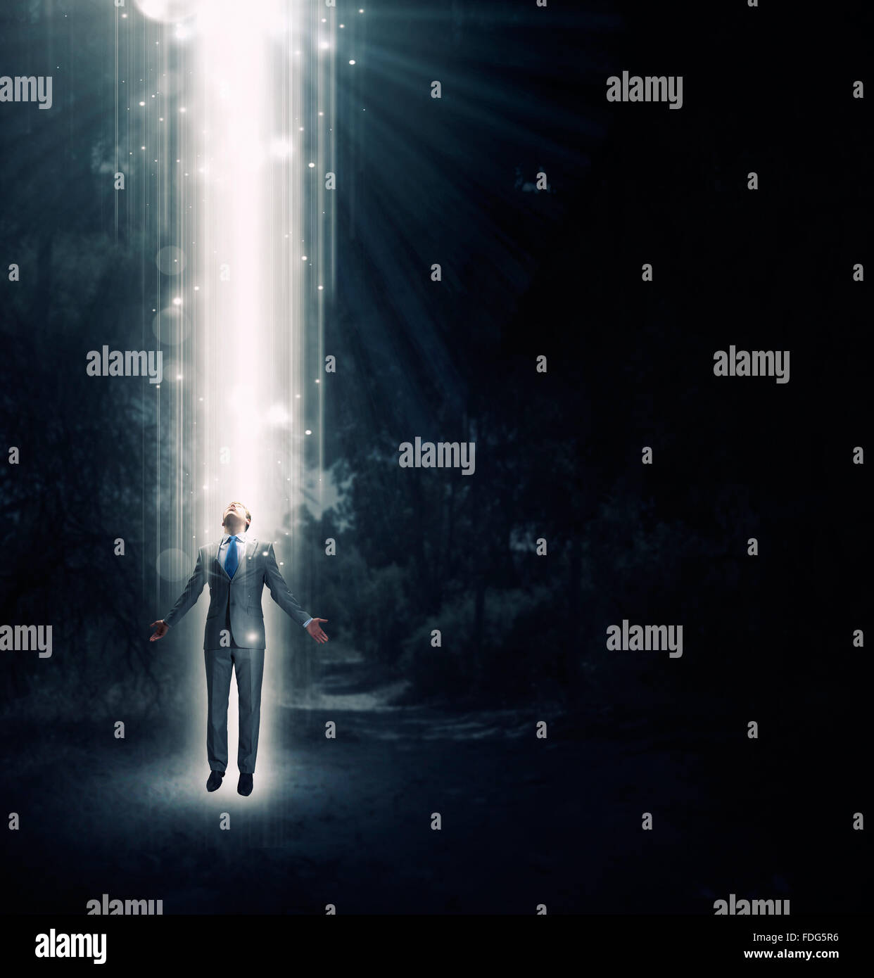 Businessman with hands spread apart standing in light coming from above ...