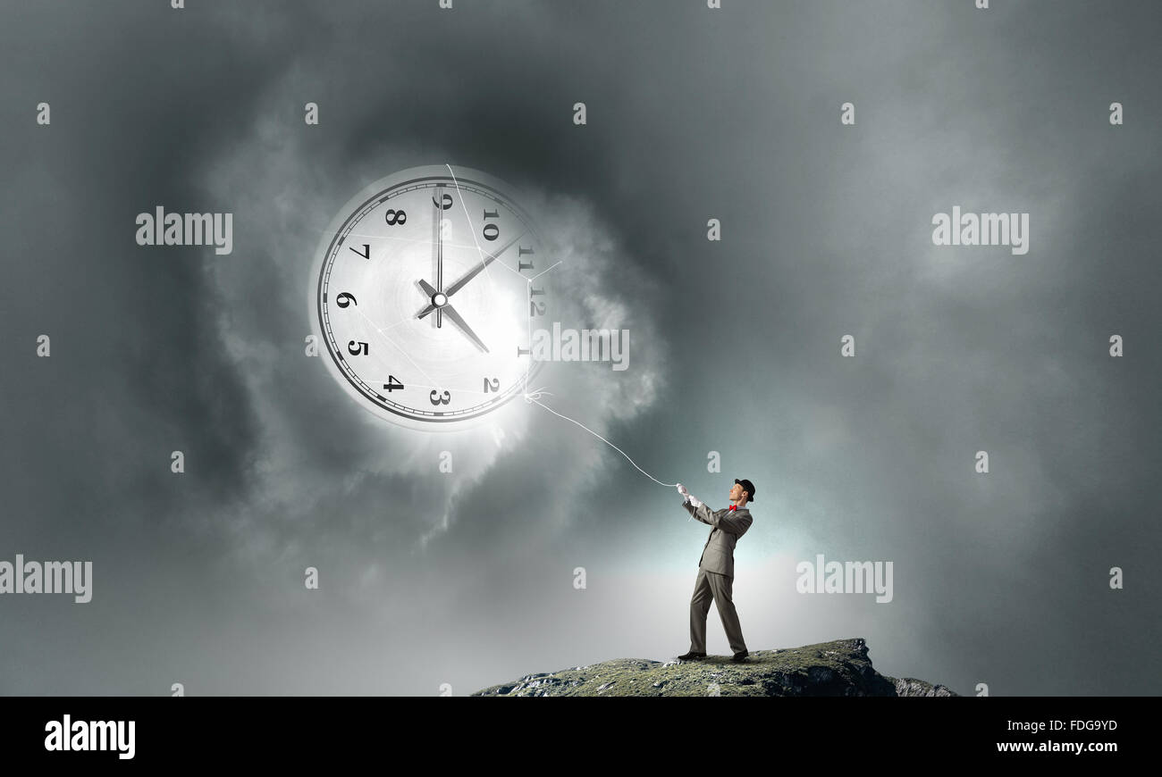 Young businessman trying to turn back time by pulling clock with rope ...