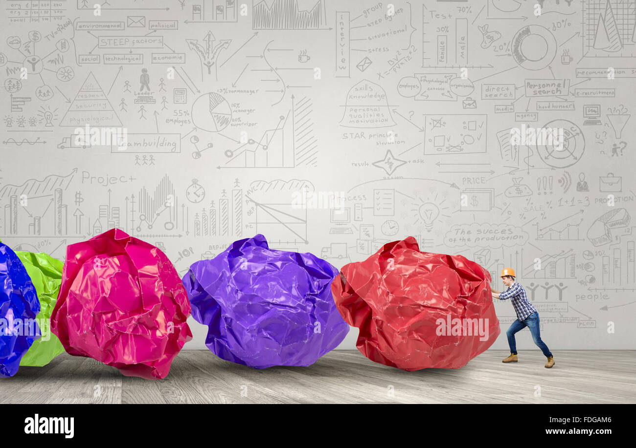 Construction man pushing big crumpled balls of colorful paper as ...