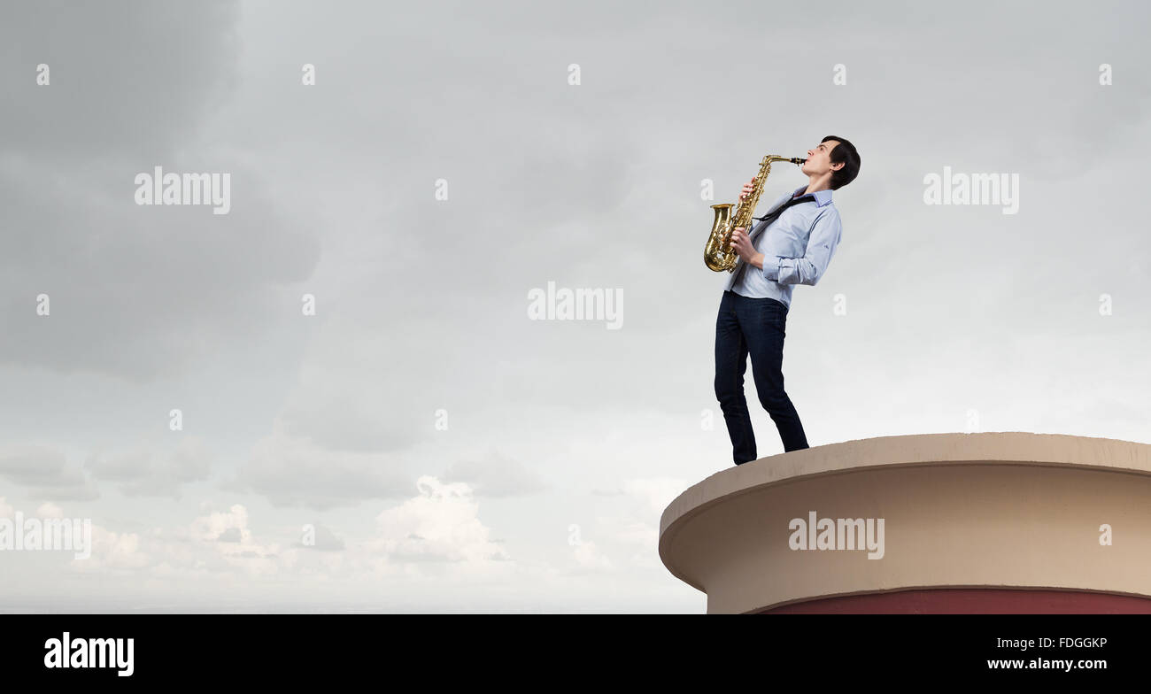 Young man on building roof playing saxophone Stock Photo - Alamy