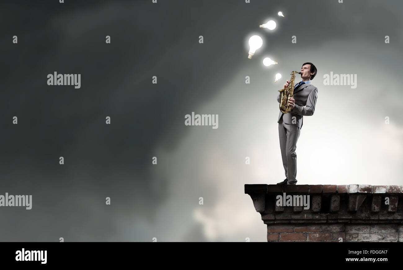 Young man on building roof playing saxophone Stock Photo - Alamy