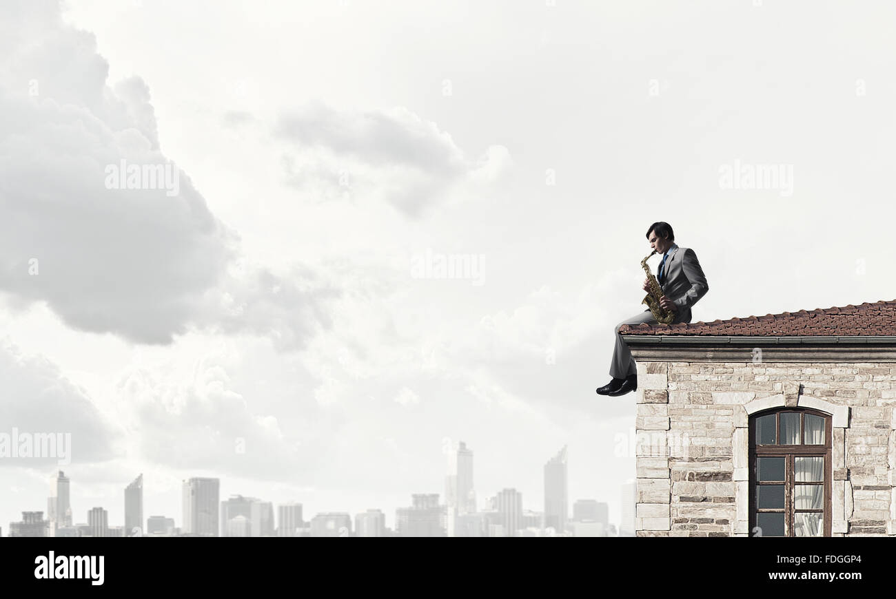 Young man sitting on roof and playing saxophone Stock Photo - Alamy