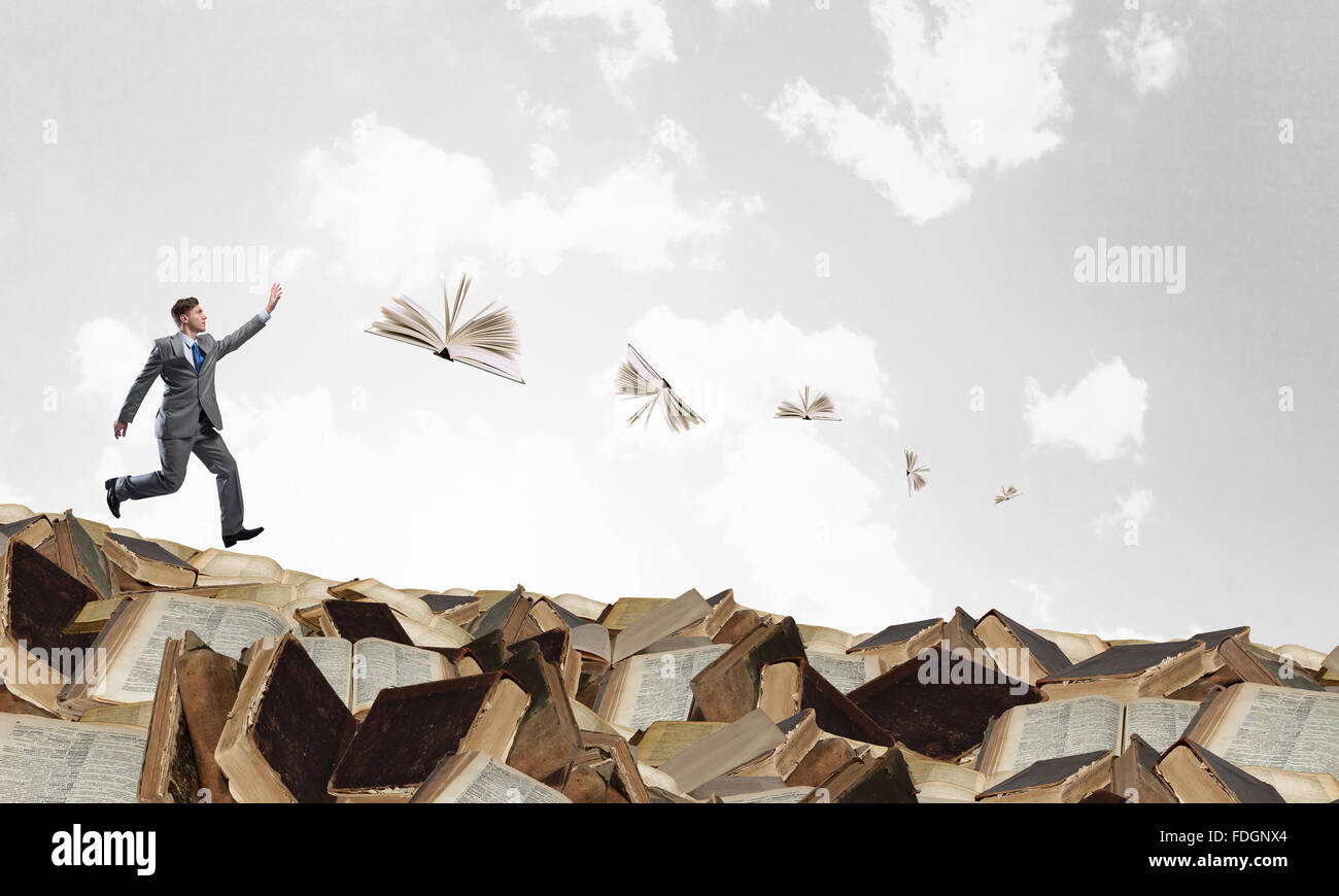 Running young businessman trying to catch book Stock Photo - Alamy