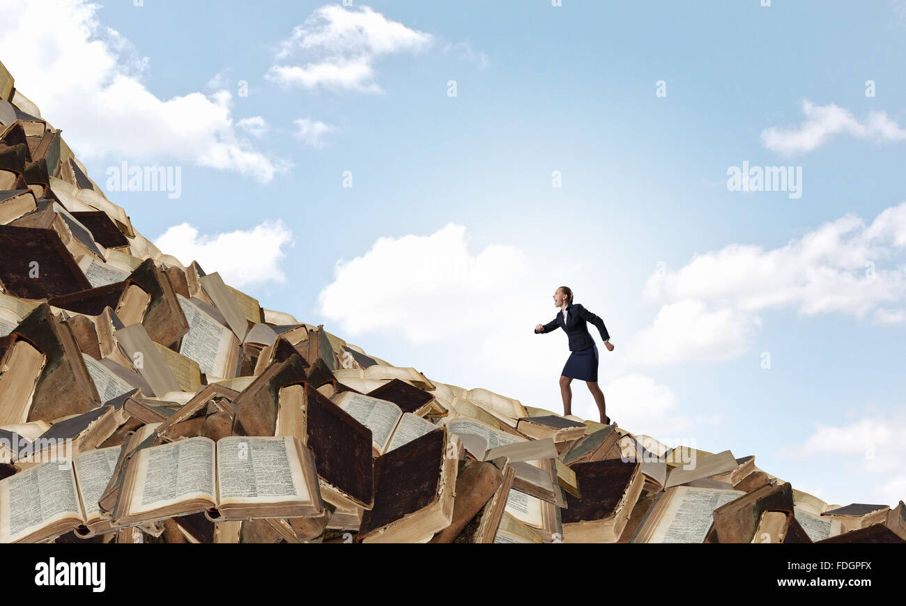 Determined businesswoman climbing up pile of books Stock Photo - Alamy