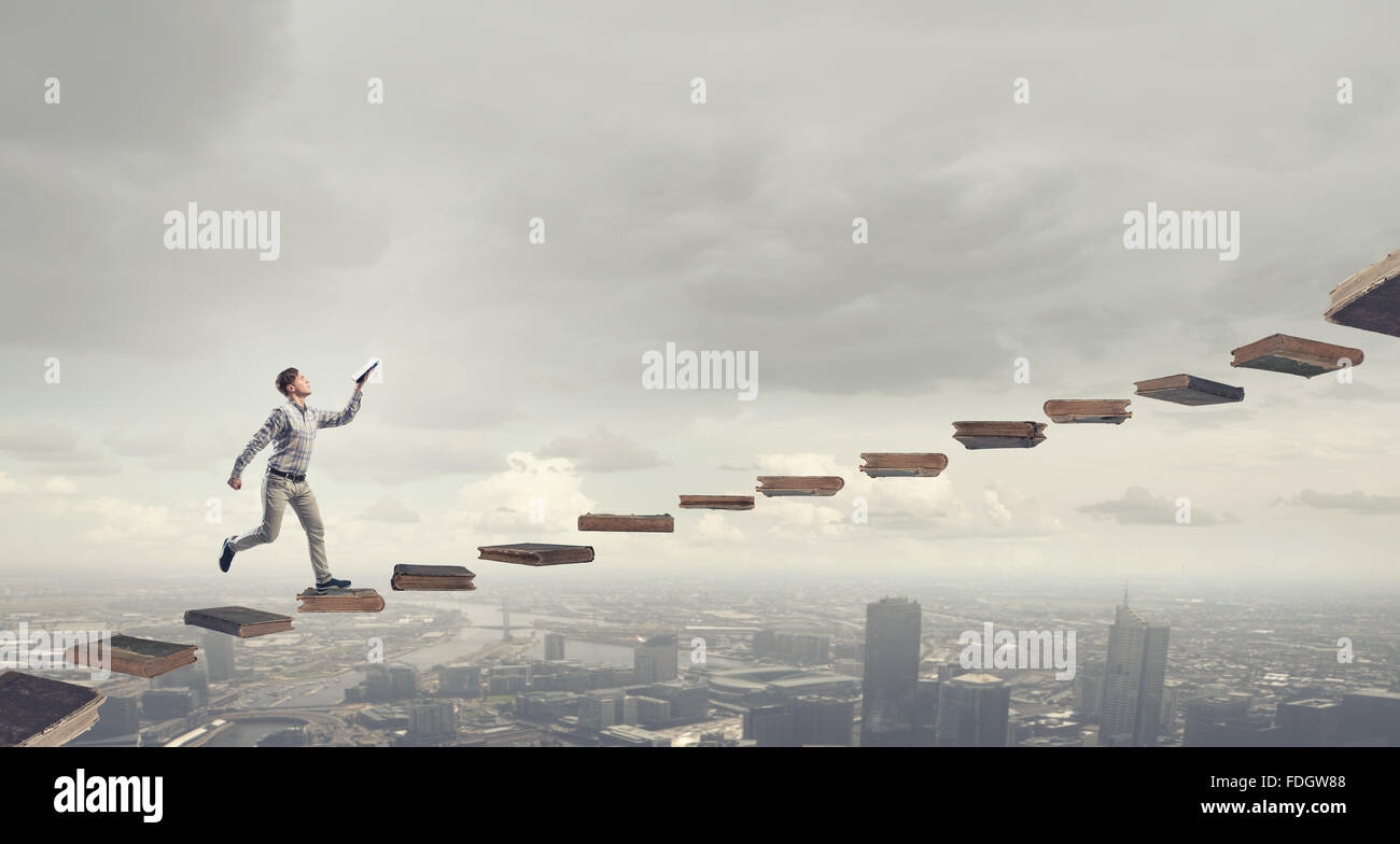 Young man running on steps reaching hand with book Stock Photo - Alamy