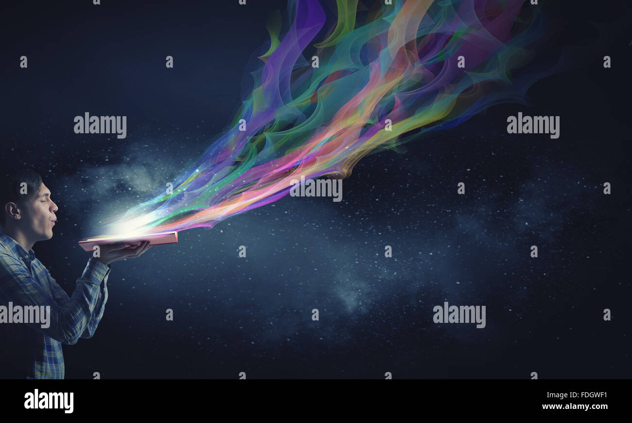 Young man with opened book in hands blowing on pages Stock Photo - Alamy