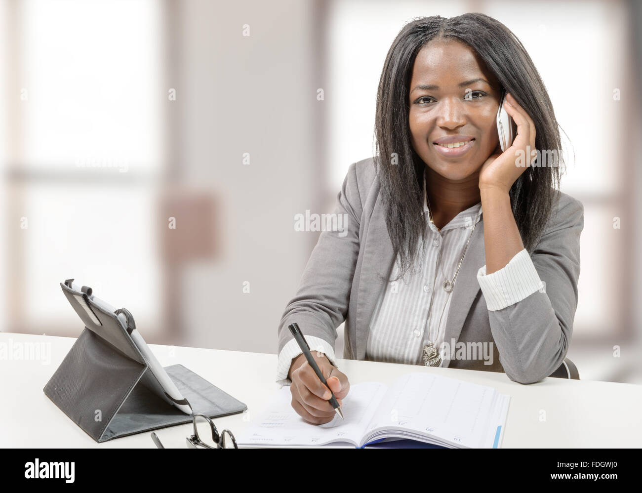a young african american woman writing, and giving a call with mobile ...