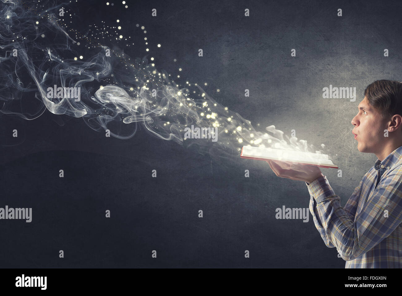 Young man with opened book in hands blowing on pages Stock Photo - Alamy