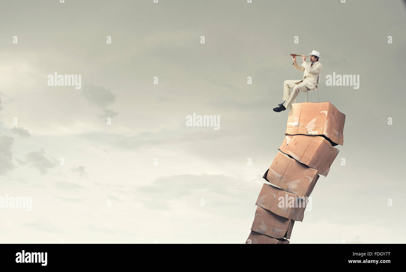 Businessman sitting on big stack of boxes looking in spyglass hi-res ...