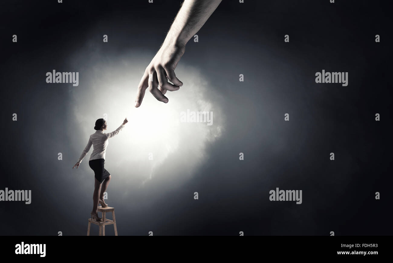 Young woman standing on chair and reaching hand to get help Stock Photo ...