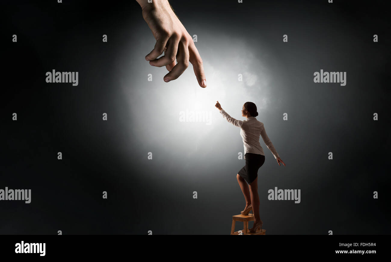 Young woman standing on chair and reaching hand to get help Stock Photo ...