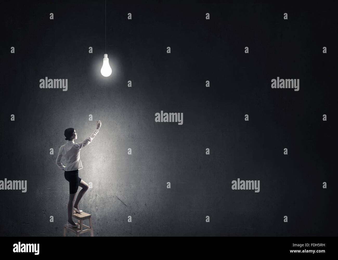 Back view of businesswoman standing on chair and reaching light bulb ...