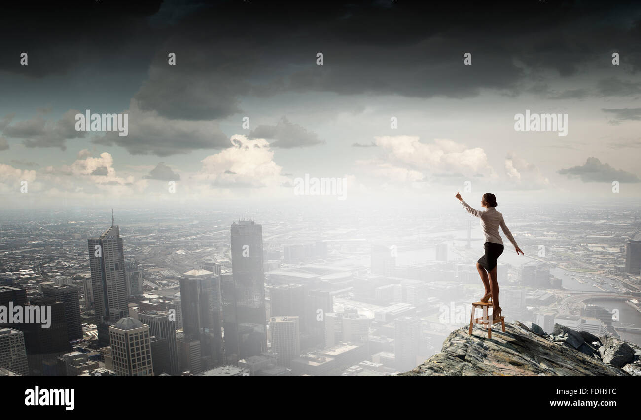 Businesswoman standing on chair and reaching hand to touch something ...