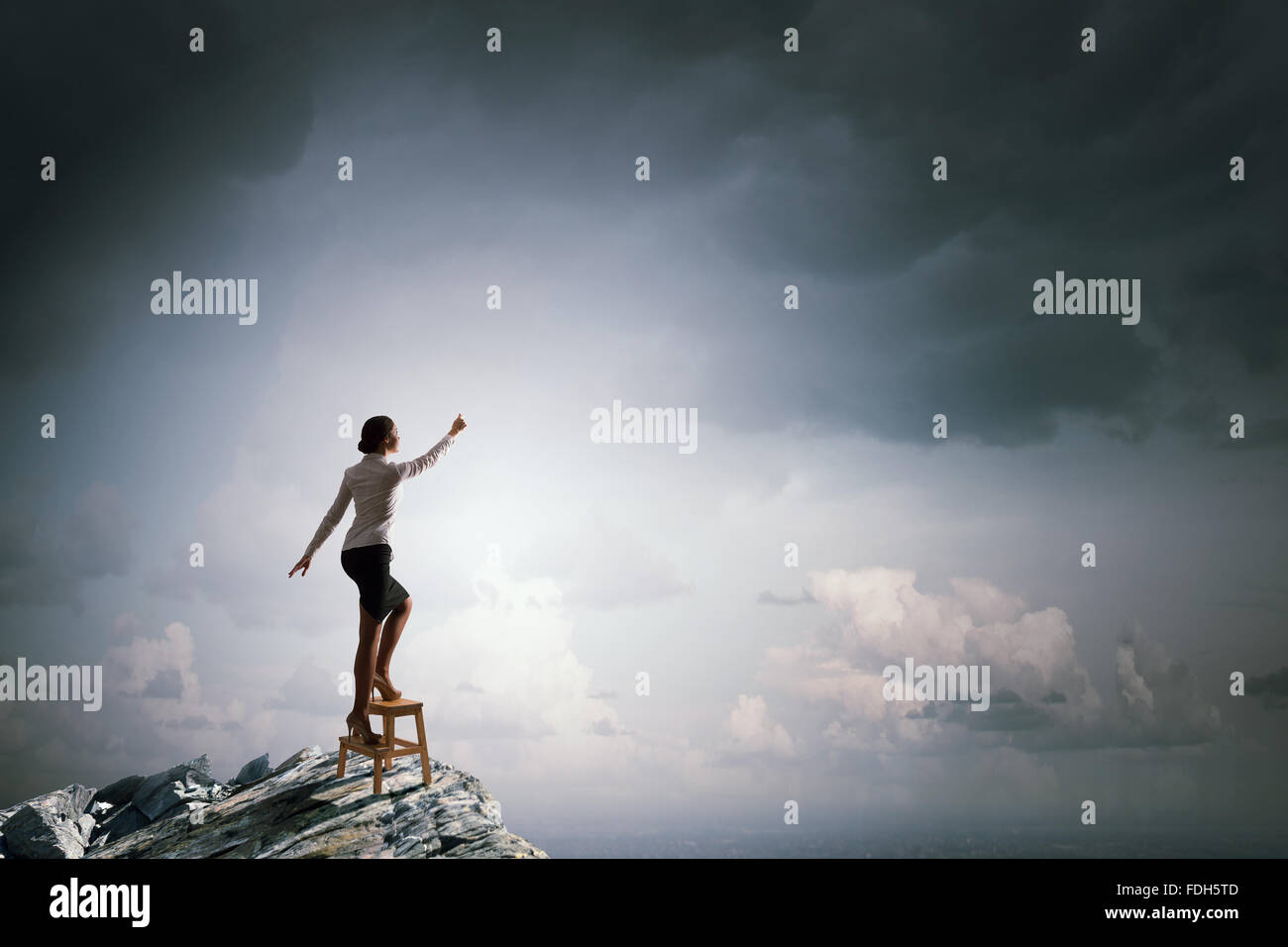 Businesswoman standing on chair and reaching hand to touch something ...