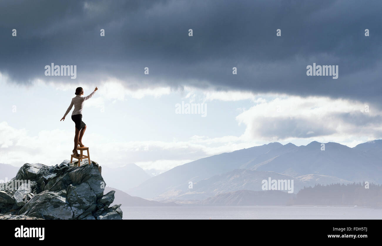 Businesswoman standing on chair and reaching hand to touch something ...