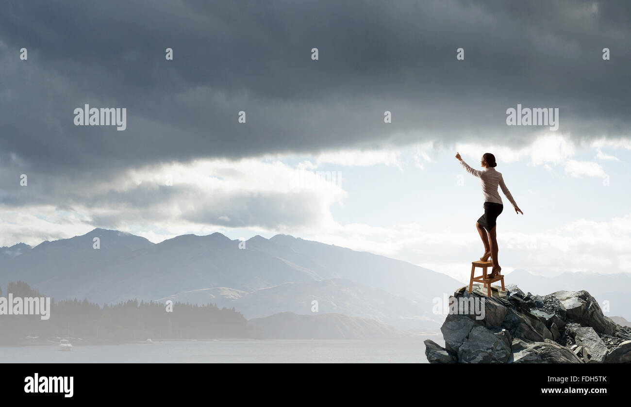 Businesswoman standing on chair and reaching hand to touch something ...