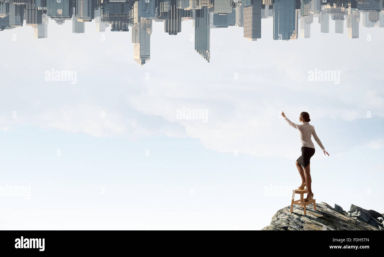 Businesswoman standing on chair and reaching hand to touch something ...