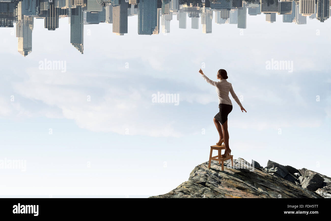 Businesswoman standing on chair and reaching hand to touch something ...
