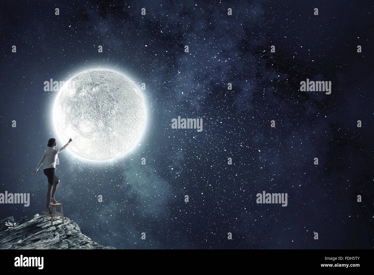 Businesswoman standing on chair and reaching hand to touch moon Stock ...