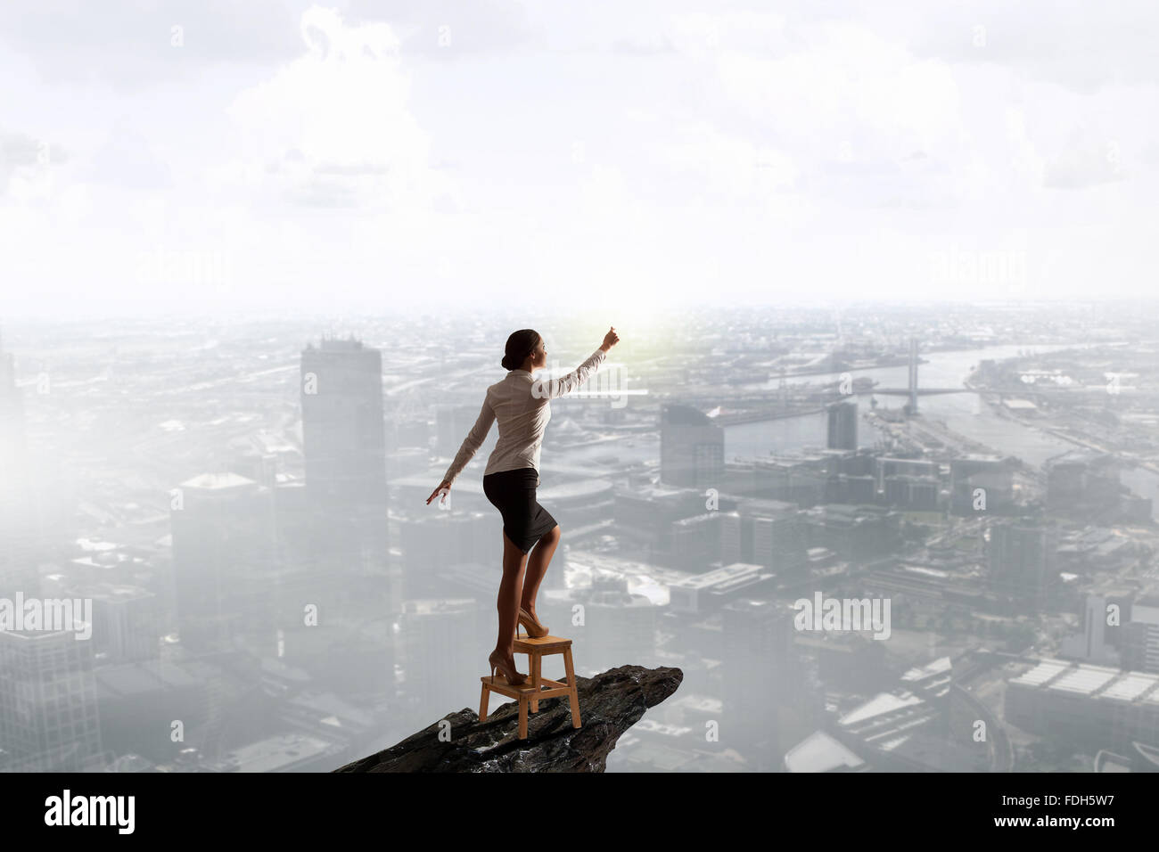 Businesswoman standing on chair and reaching hand to touch something ...