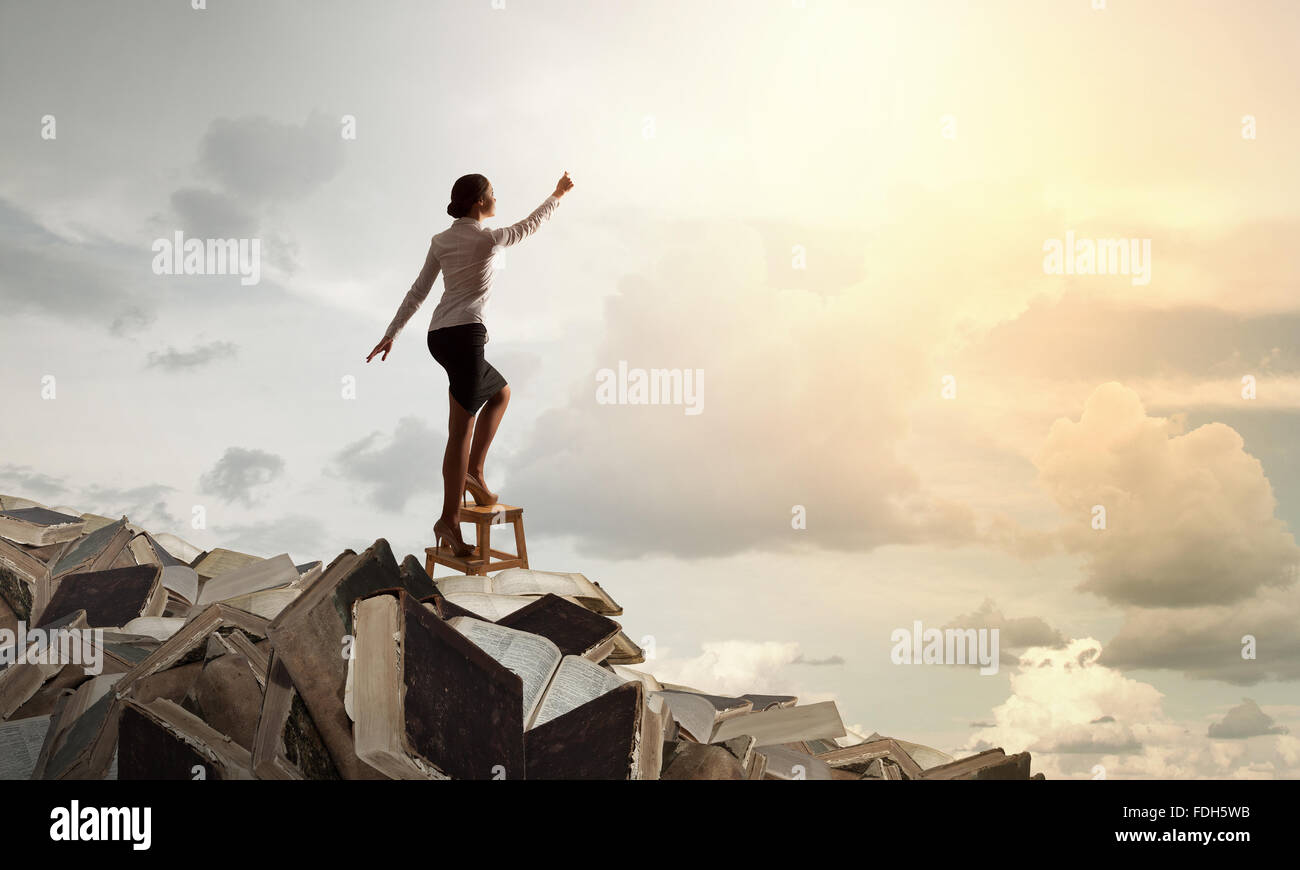 Businesswoman standing on chair and reaching hand to touch something ...