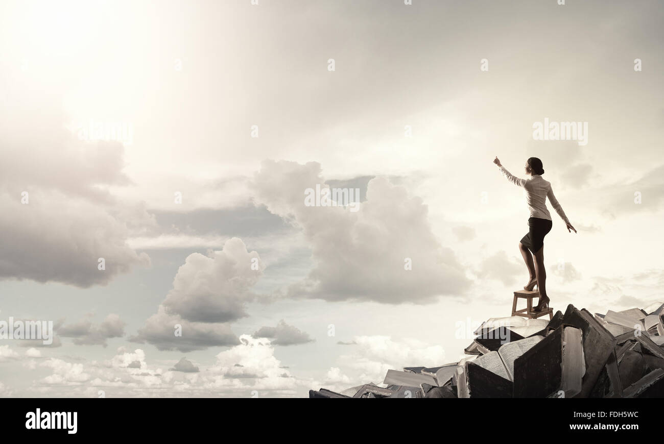 Businesswoman standing on chair and reaching hand to touch something ...