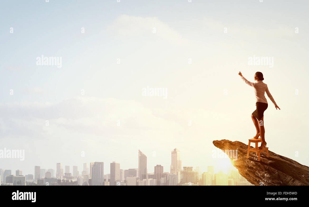 Businesswoman standing on chair and reaching hand to touch something ...