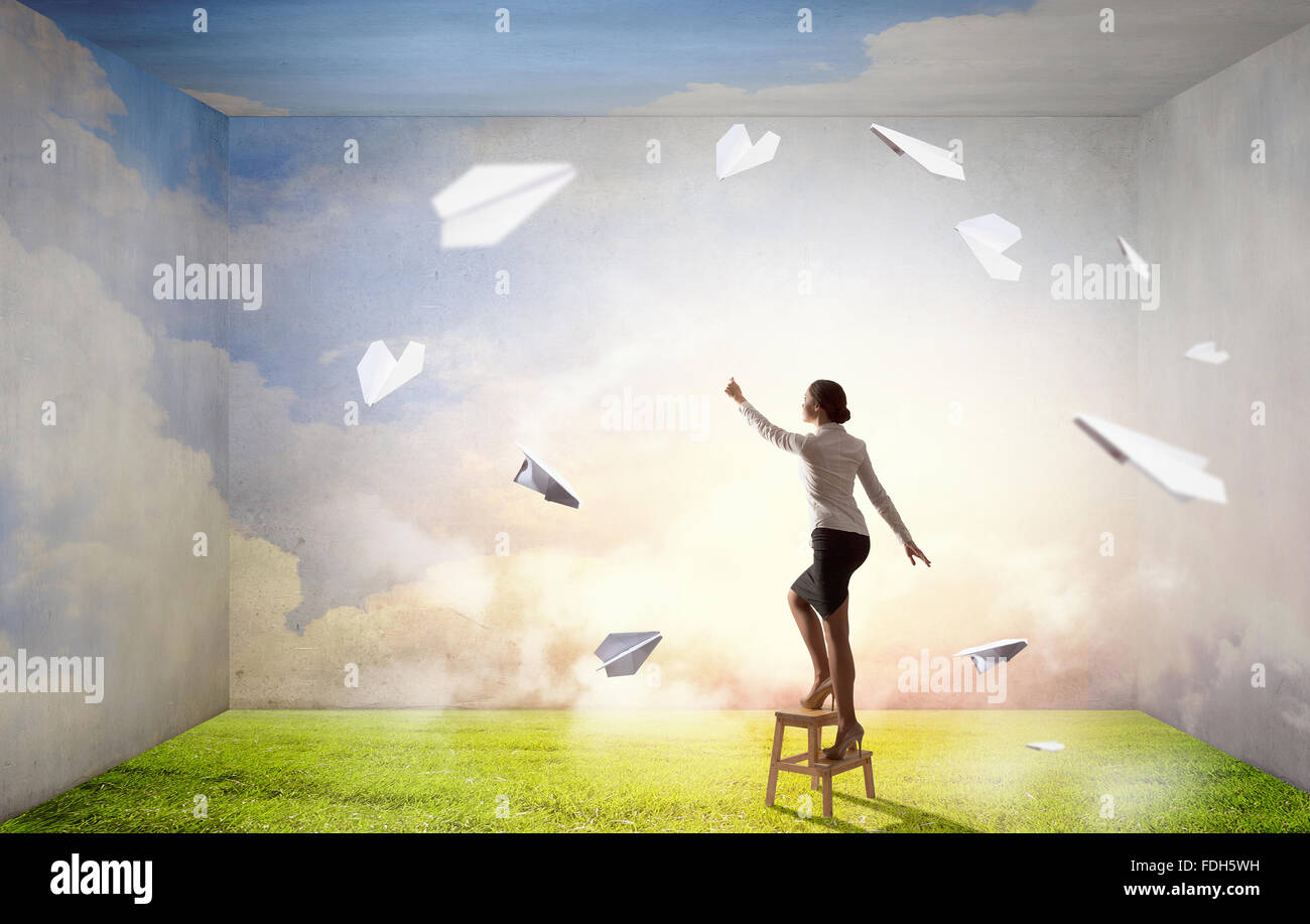 Businesswoman standing on chair and reaching hand to touch something ...