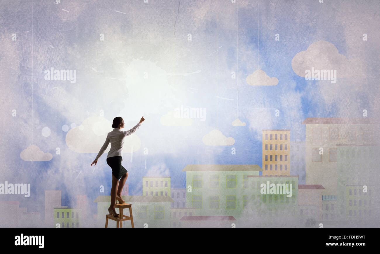 Businesswoman standing on chair and reaching hand to touch something ...