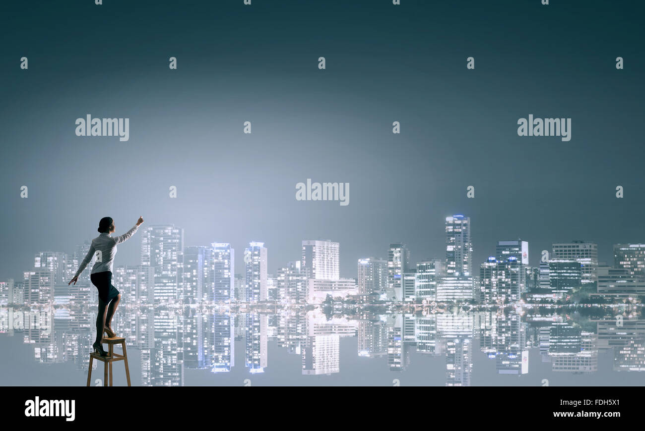 Businesswoman standing on chair and reaching hand to touch something ...