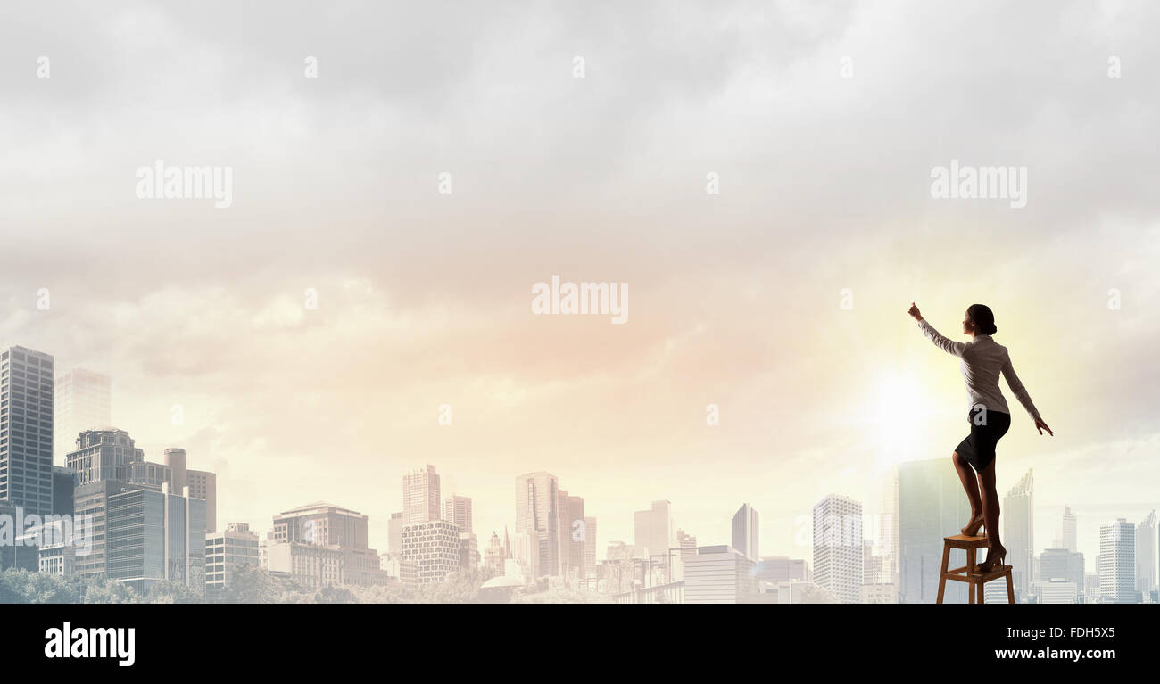 Businesswoman standing on chair and reaching hand to touch something ...