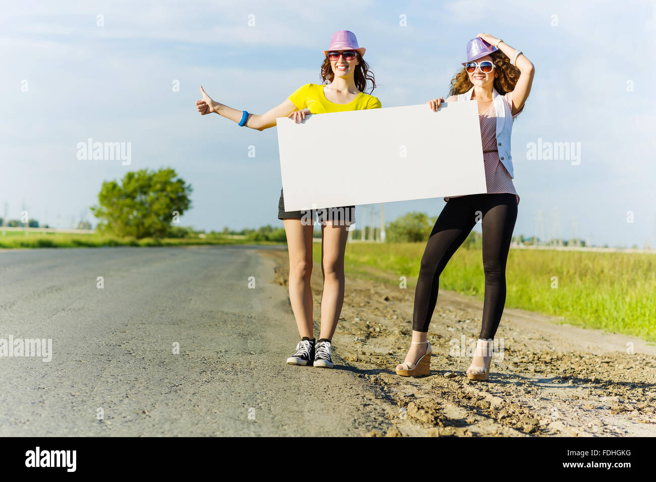 Two pretty young girls standing aside road with blank white banner ...