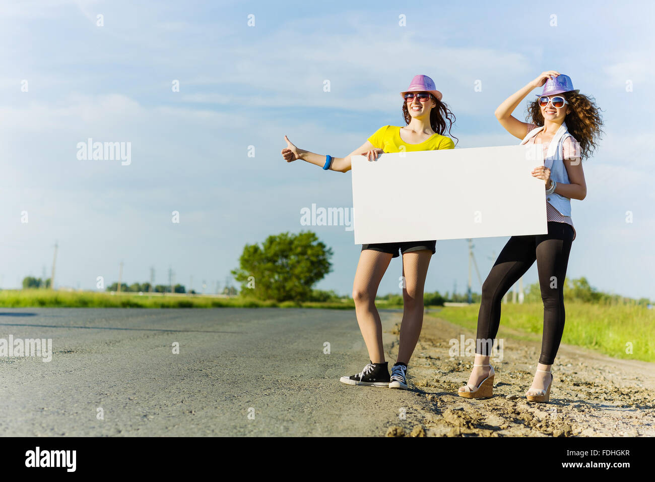 Two pretty young girls standing aside road with blank white banner ...