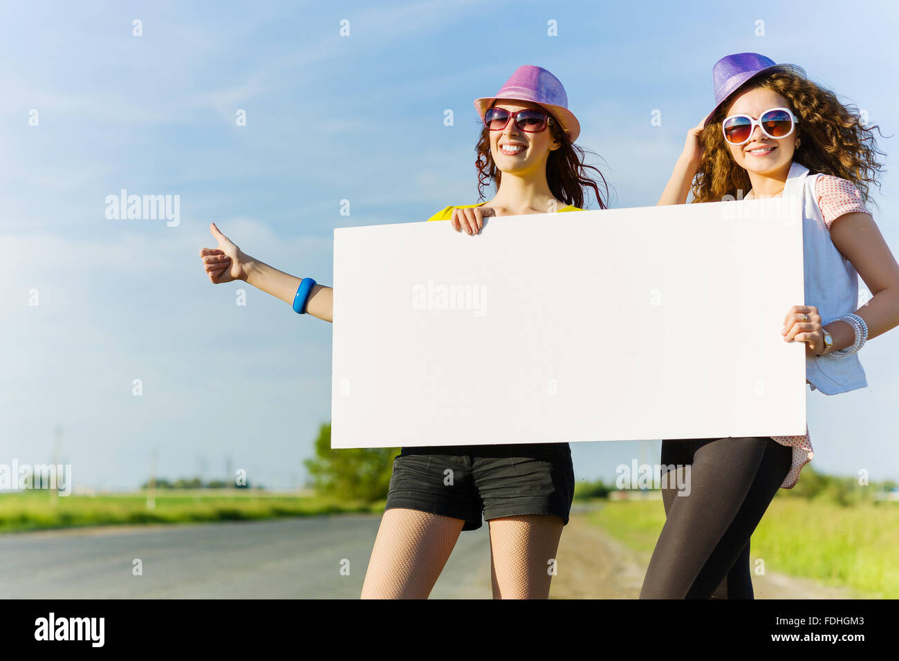 Two pretty young girls standing aside road with blank white banner ...