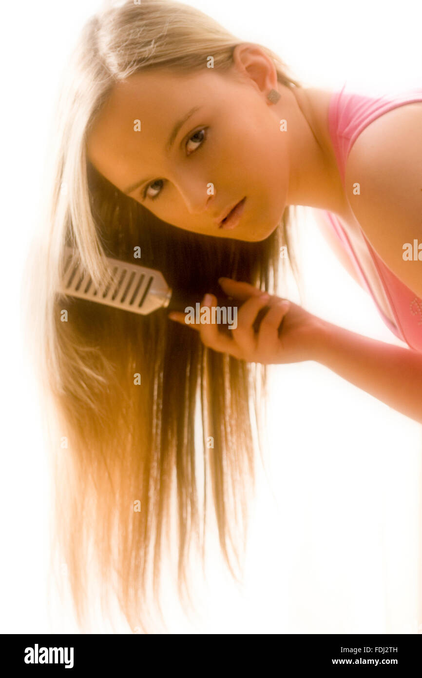 Teenage girl, bending forward, backlit, brushing her long blonde hair ...