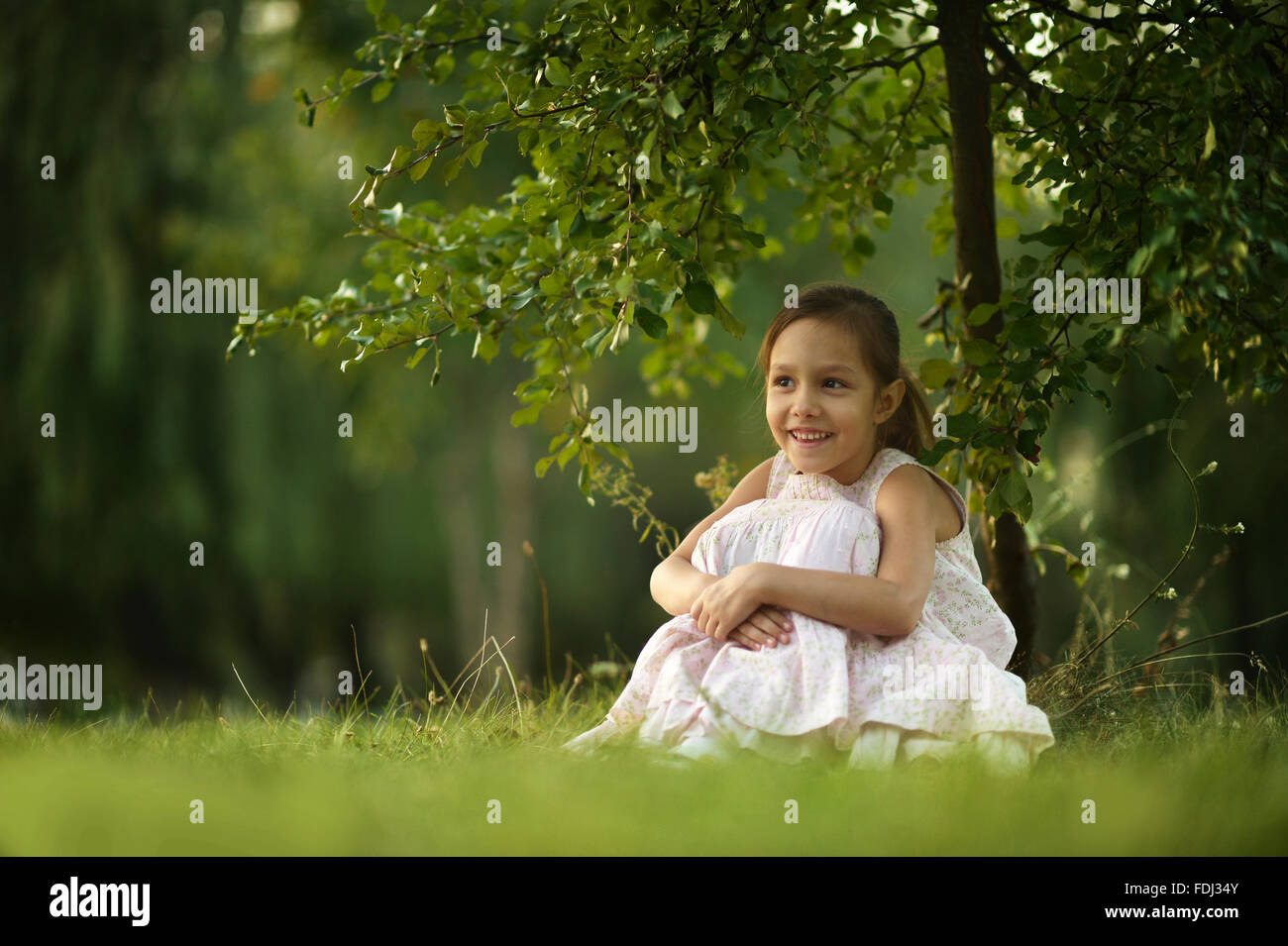 Little girl sitting under a tree in nature Stock Photo - Alamy