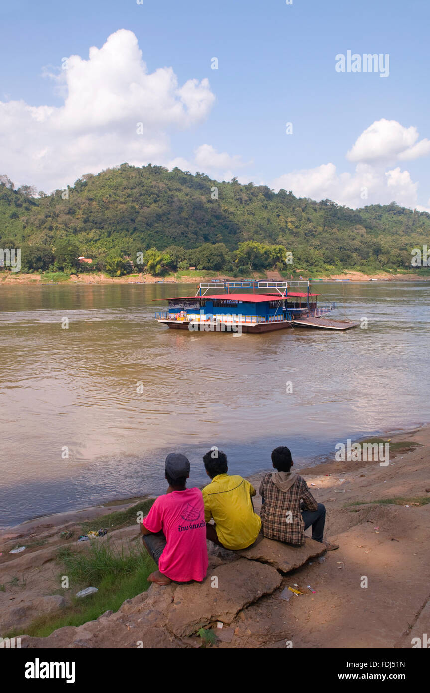 Young men watching a ferry on the Mekong River in Luang Prabang, Laos ...