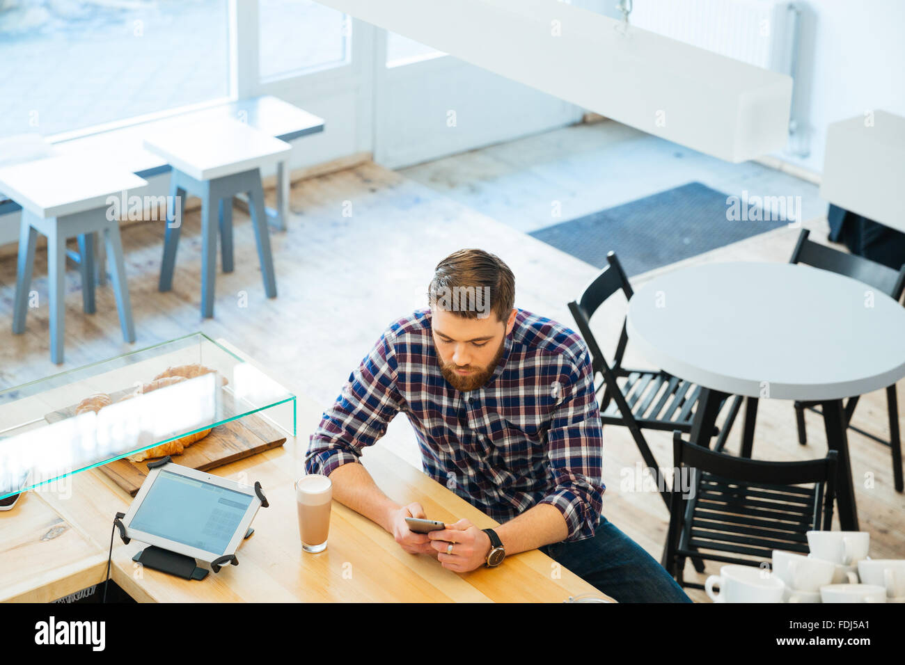 Casual man sitting at the table in coffee shop and using smartphone ...