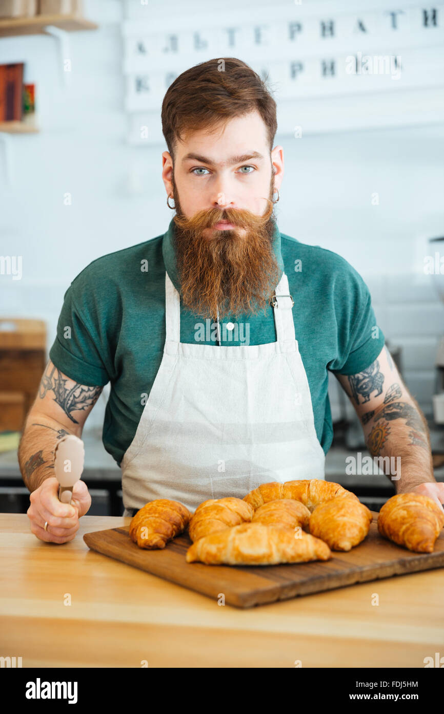 Portrait of handsome bearded man barista with croissants in coffee shop ...