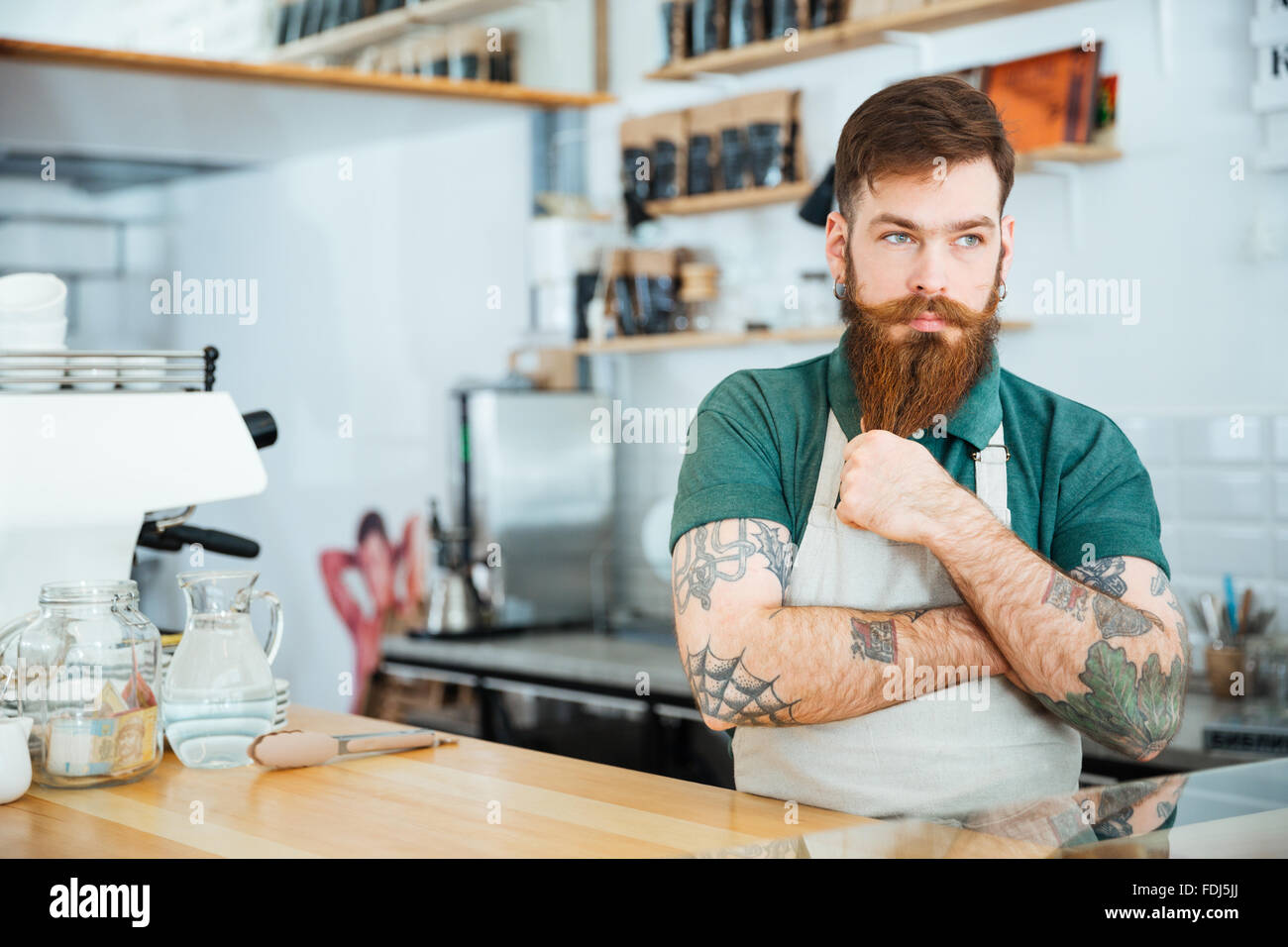 Handsome pensive man barista touching his beard and thinking in coffee ...