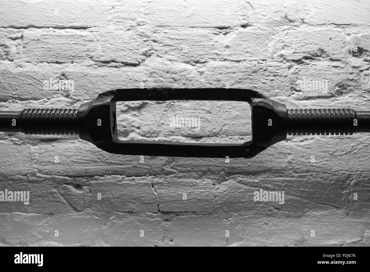 Old black turnbuckle, close-up photo over white brick wall background ...